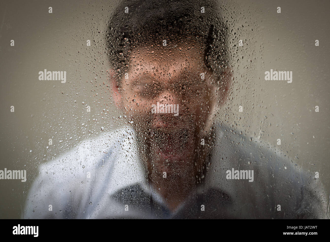 Young man is screaming, behind a blurred window with drops, gray ...