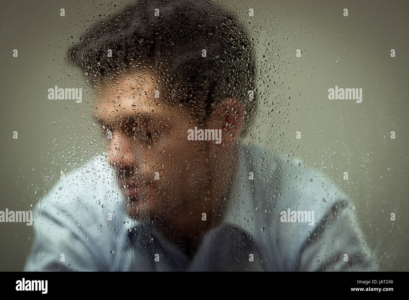 Worry depresed young man, behind a blurred window with drops, gray ...