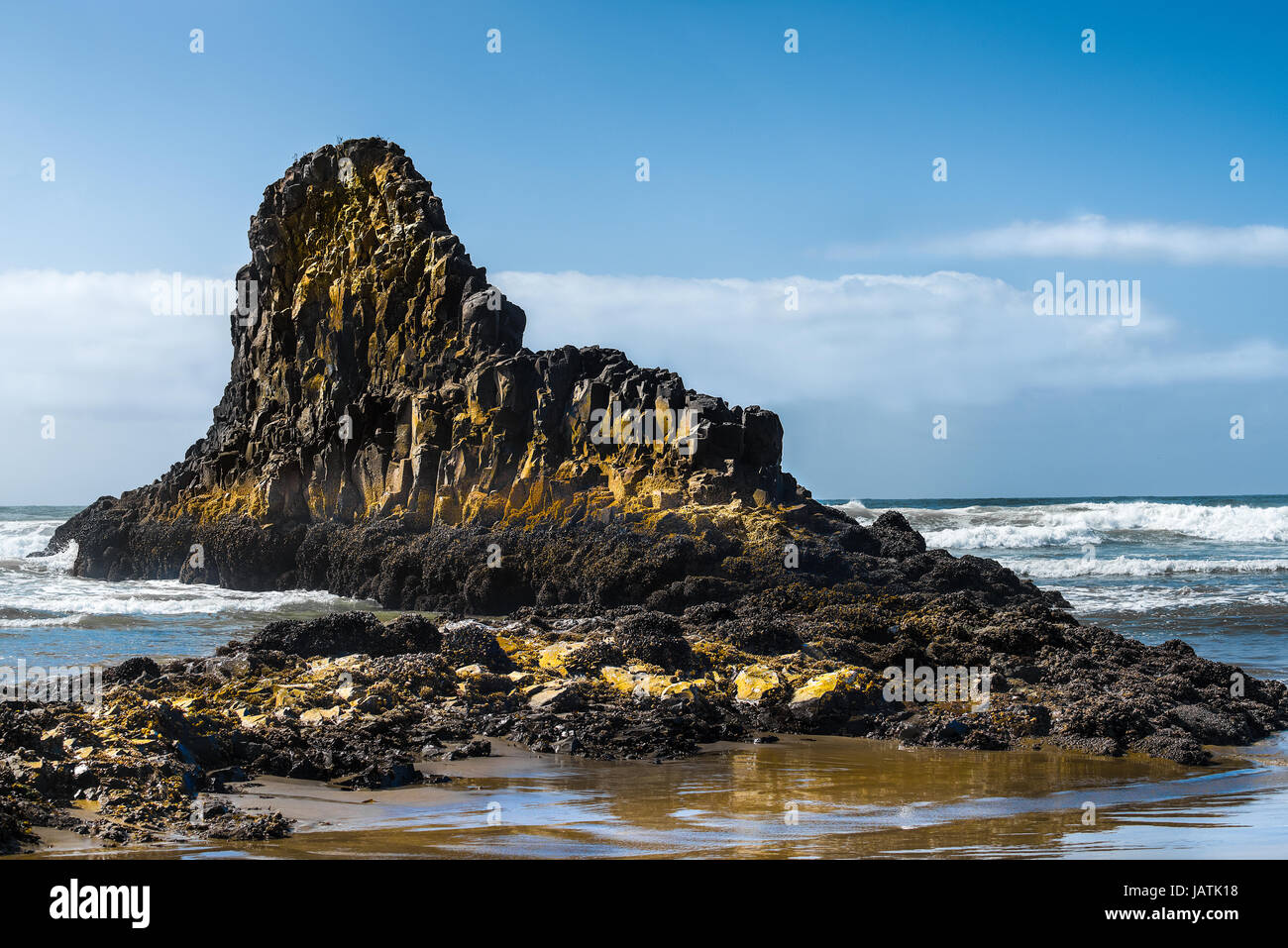 A large rock formation on the beach shines with color from the light ...
