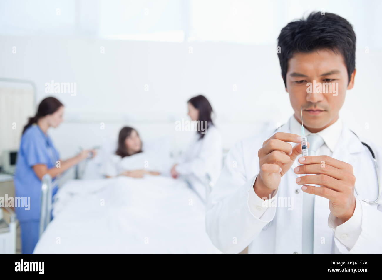 Doctor preparing a syringe while his colleagues are treating a patient ...
