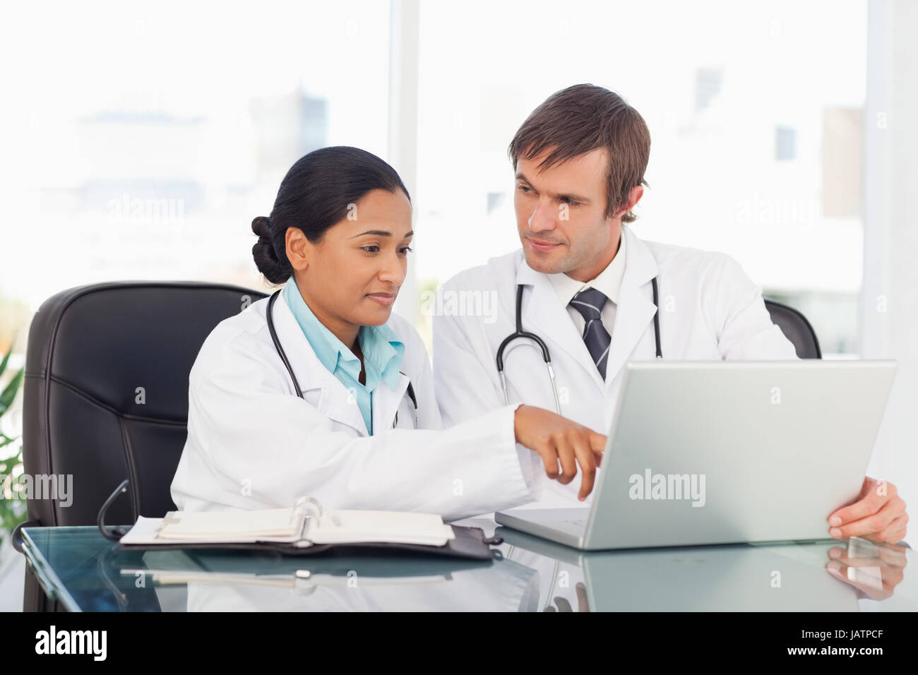 Serious doctor pointing at the screen of the laptop while talking to ...