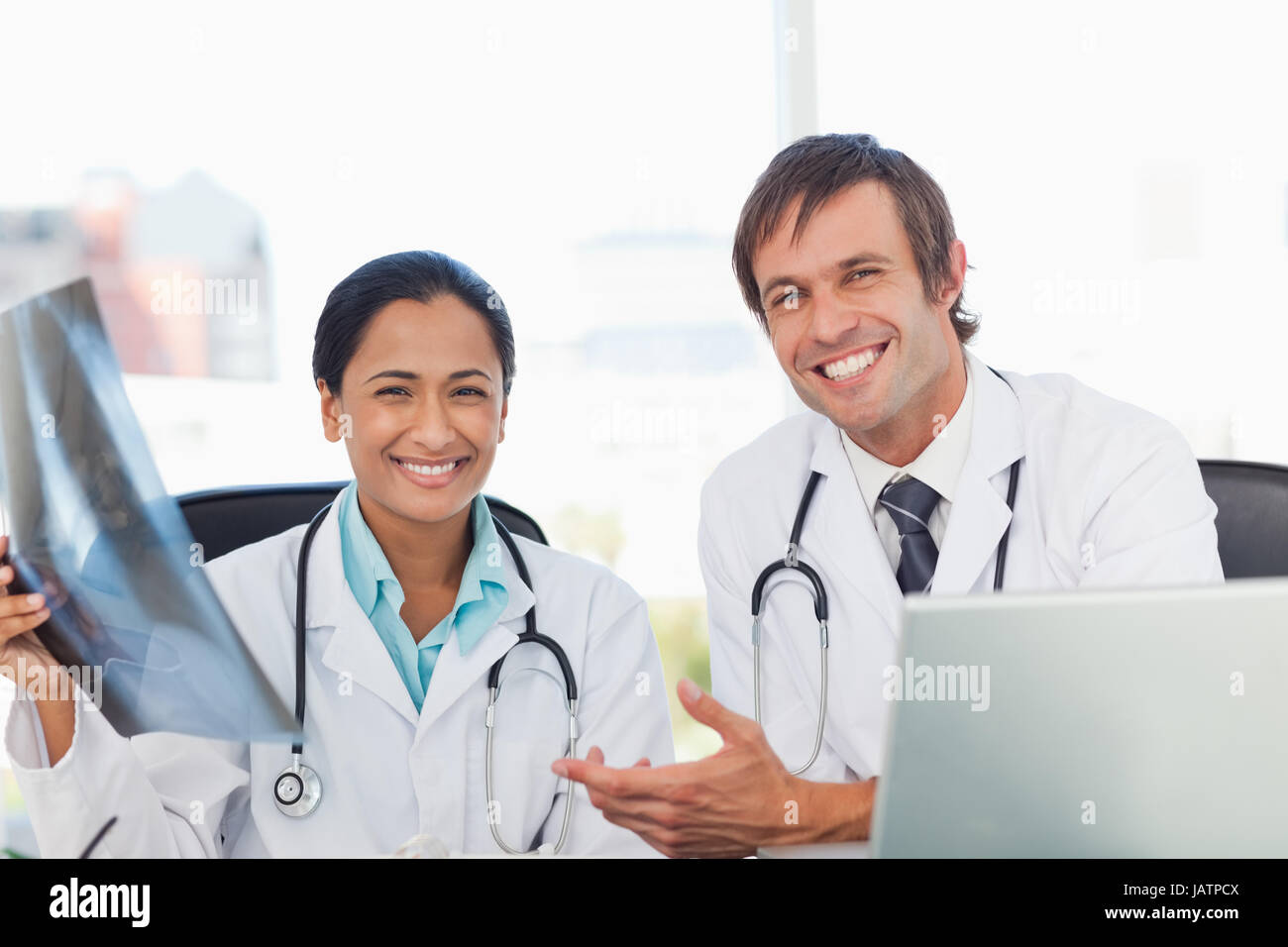 Smiling doctors looking at the camera while sitting at a desk Stock ...