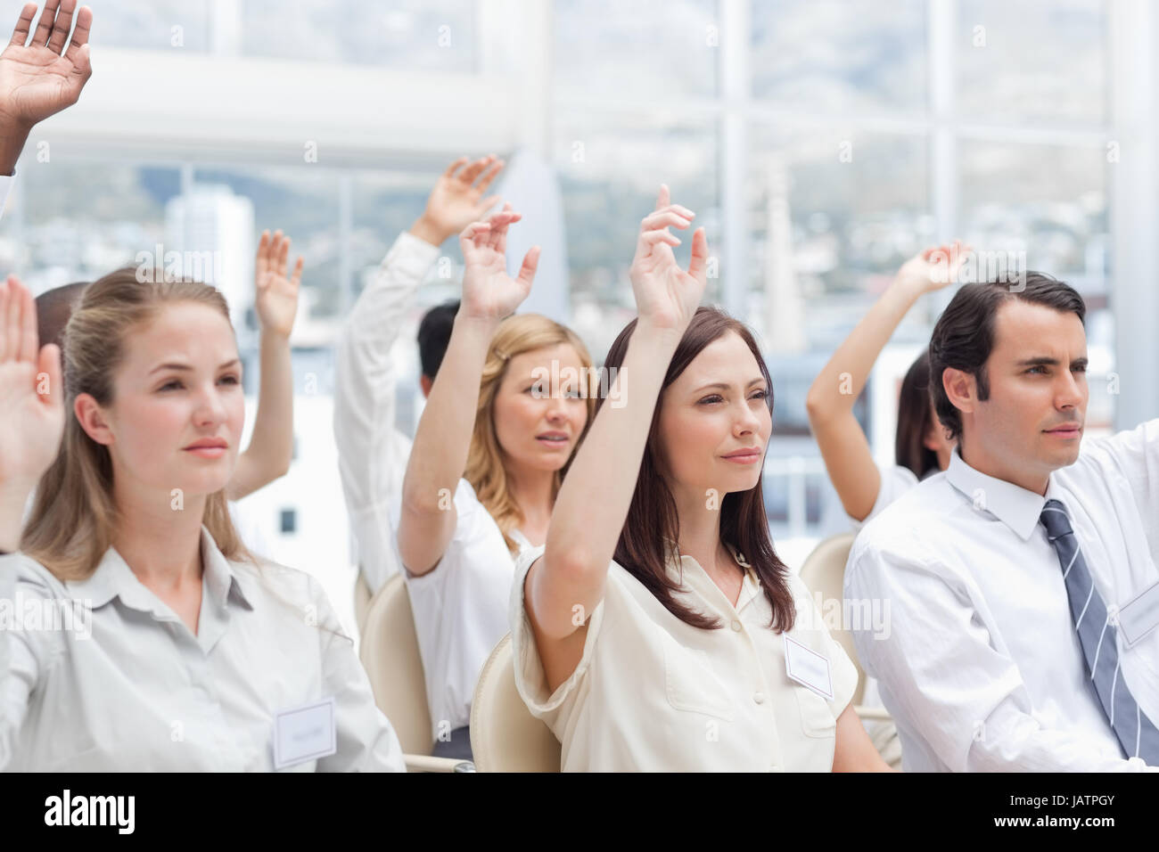 Serious colleagues raising their hands as they sit together Stock Photo ...