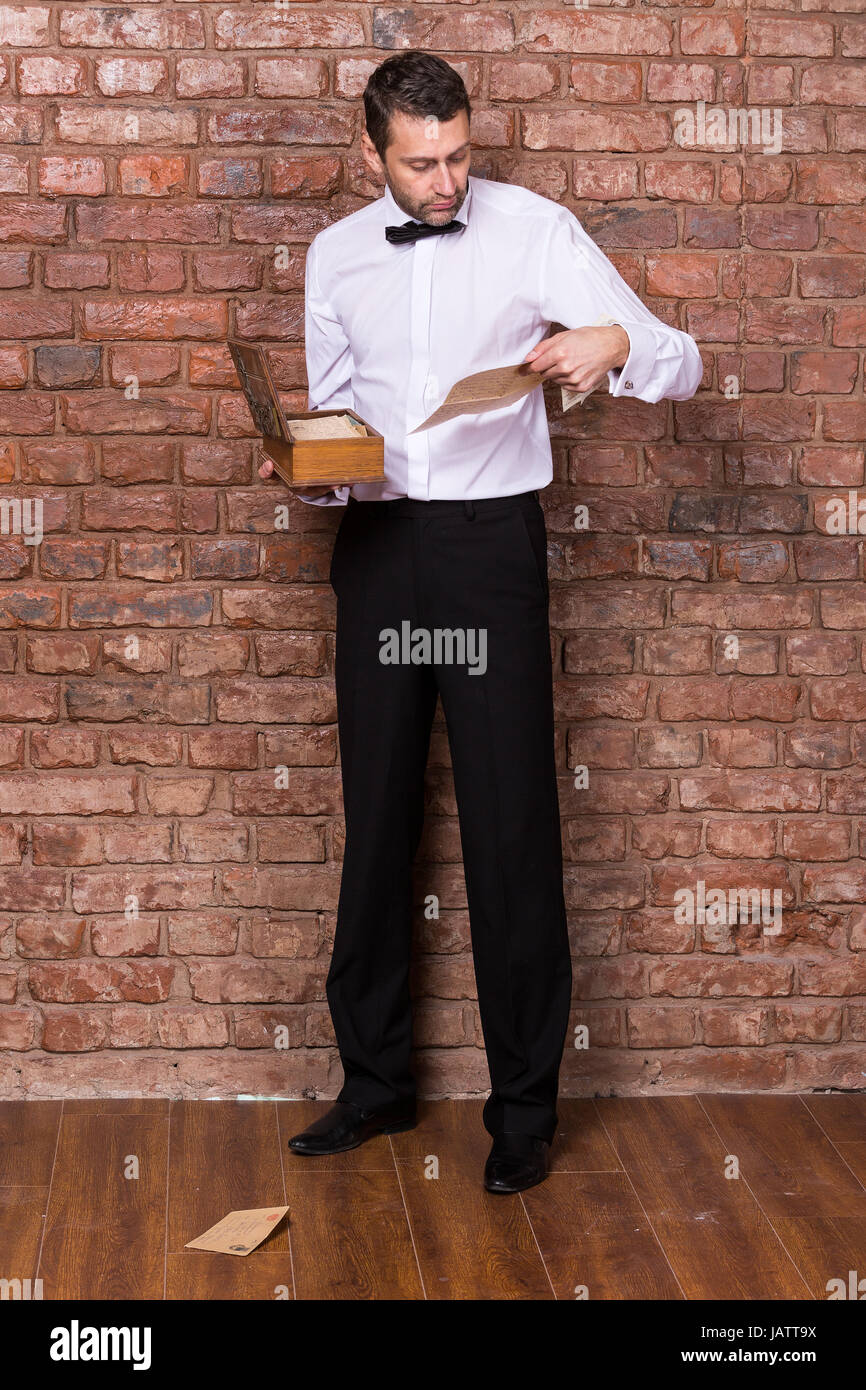 Man standing reading a old document from a wooden box which he is ...