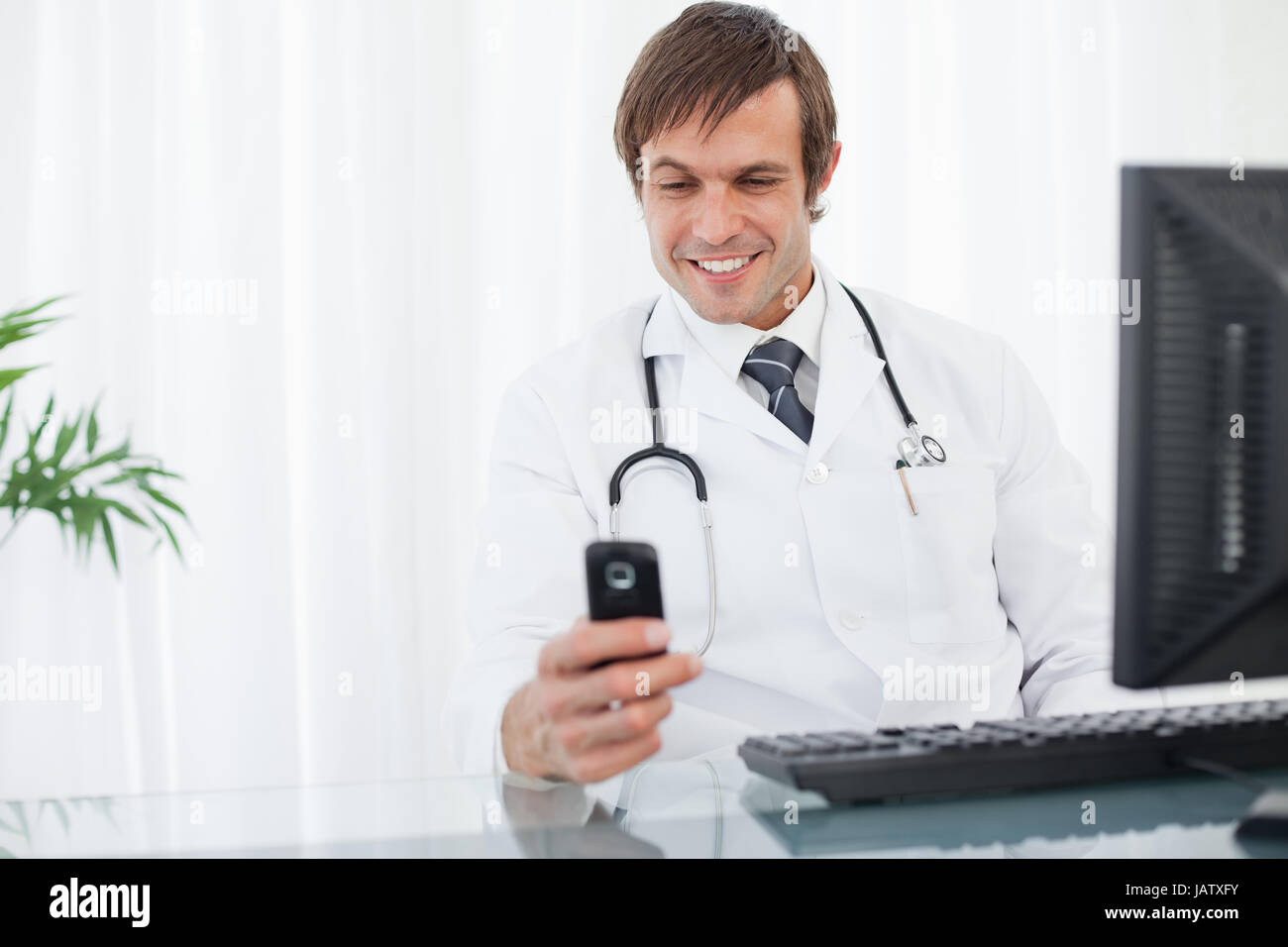 Smiling doctor looking at his mobile phone Stock Photo - Alamy