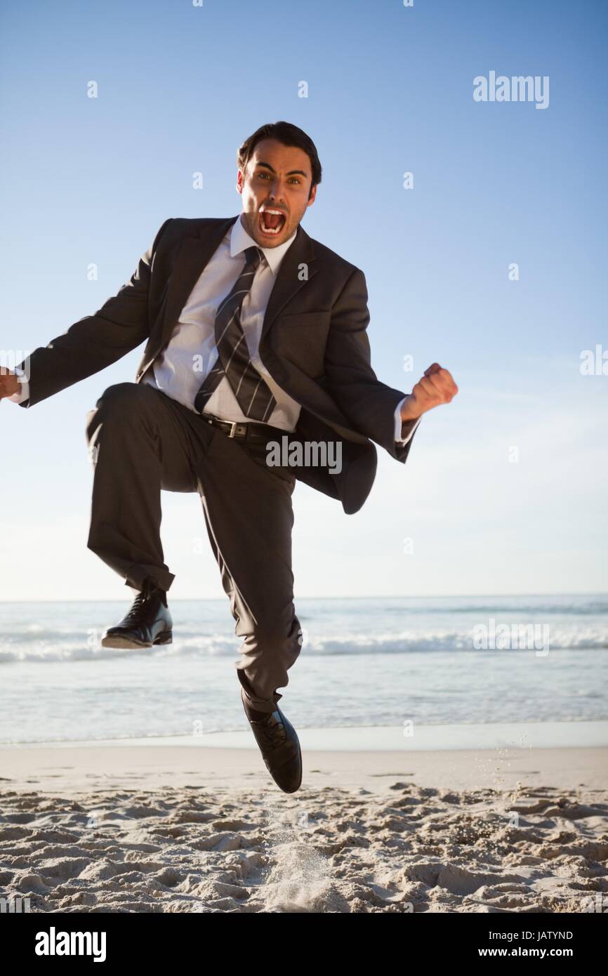 Young businessman shouting while jumping on the beach Stock Photo - Alamy