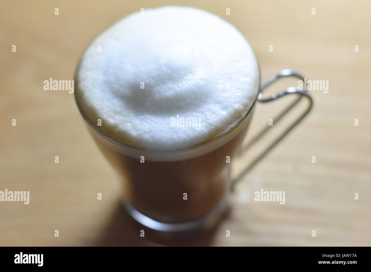 Frothy cream atop a cappuchino in an Italian glass cup with stainless ...