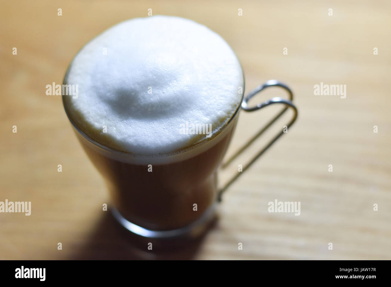 Frothy cream atop a cappuchino in an Italian glass cup with stainless ...