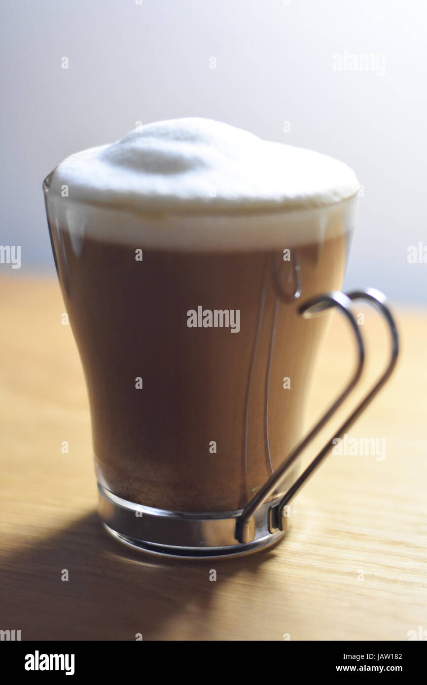 Frothy cream atop a cappuchino in an Italian glass cup with stainless ...