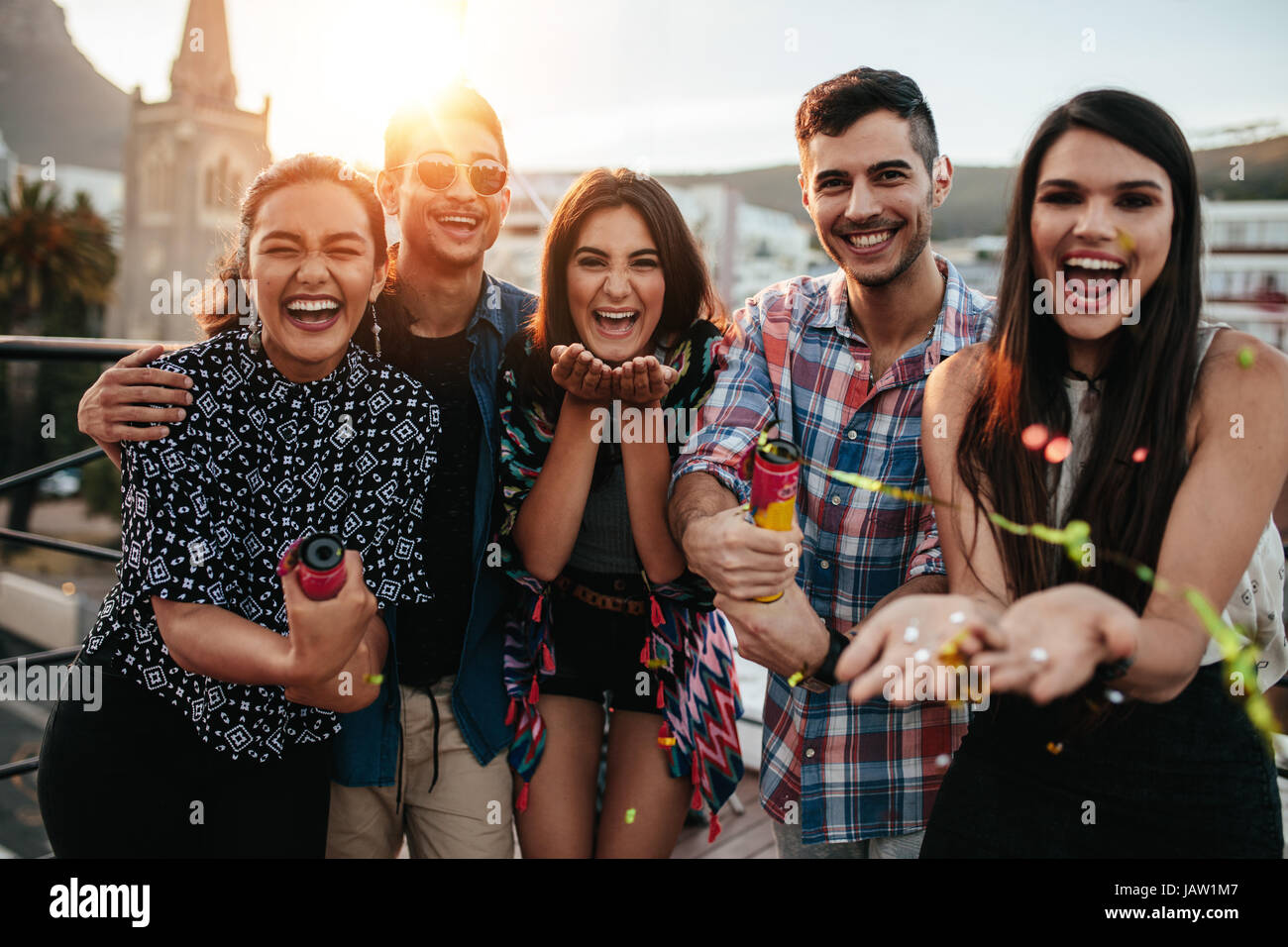 Smiling young people throwing confetti on a rooftop party. Best friends ...