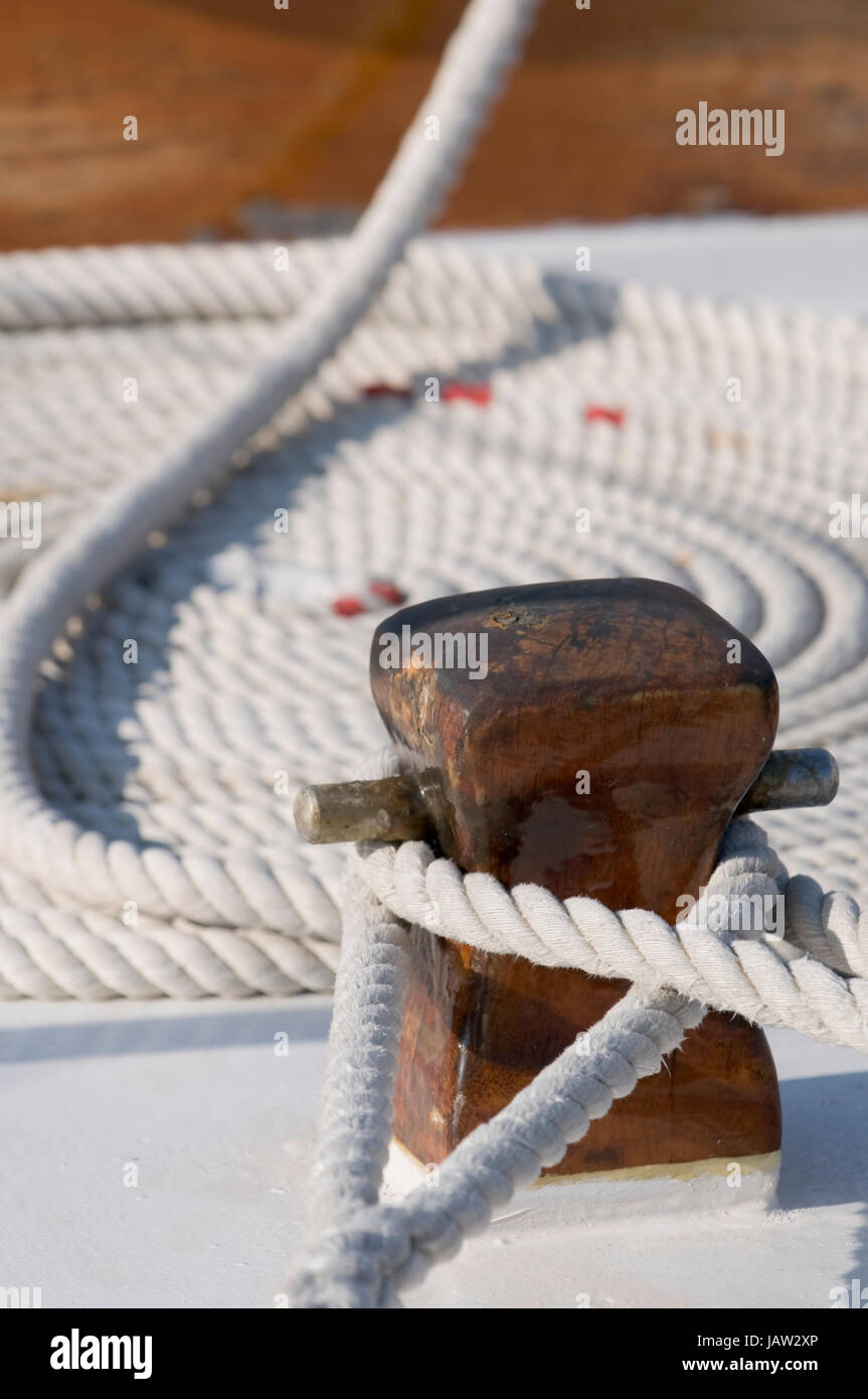 Detail of a sailboat deck with two ropes tied up on a bitt and one ...