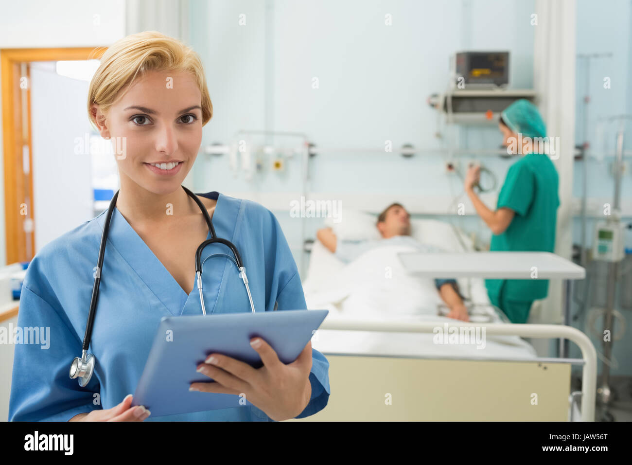 Blonde nurse holding a tablet computer while smiling in hospital ward ...