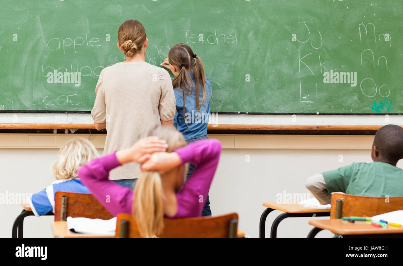 Back view of elementary teacher and pupil writing on blackboard Stock ...