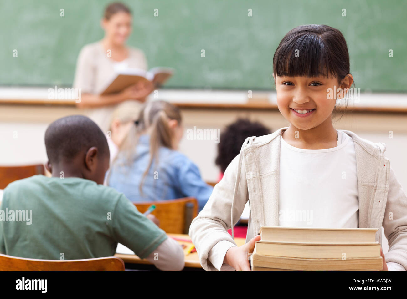 Smiling elementary student with books standing in classroom Stock Photo ...