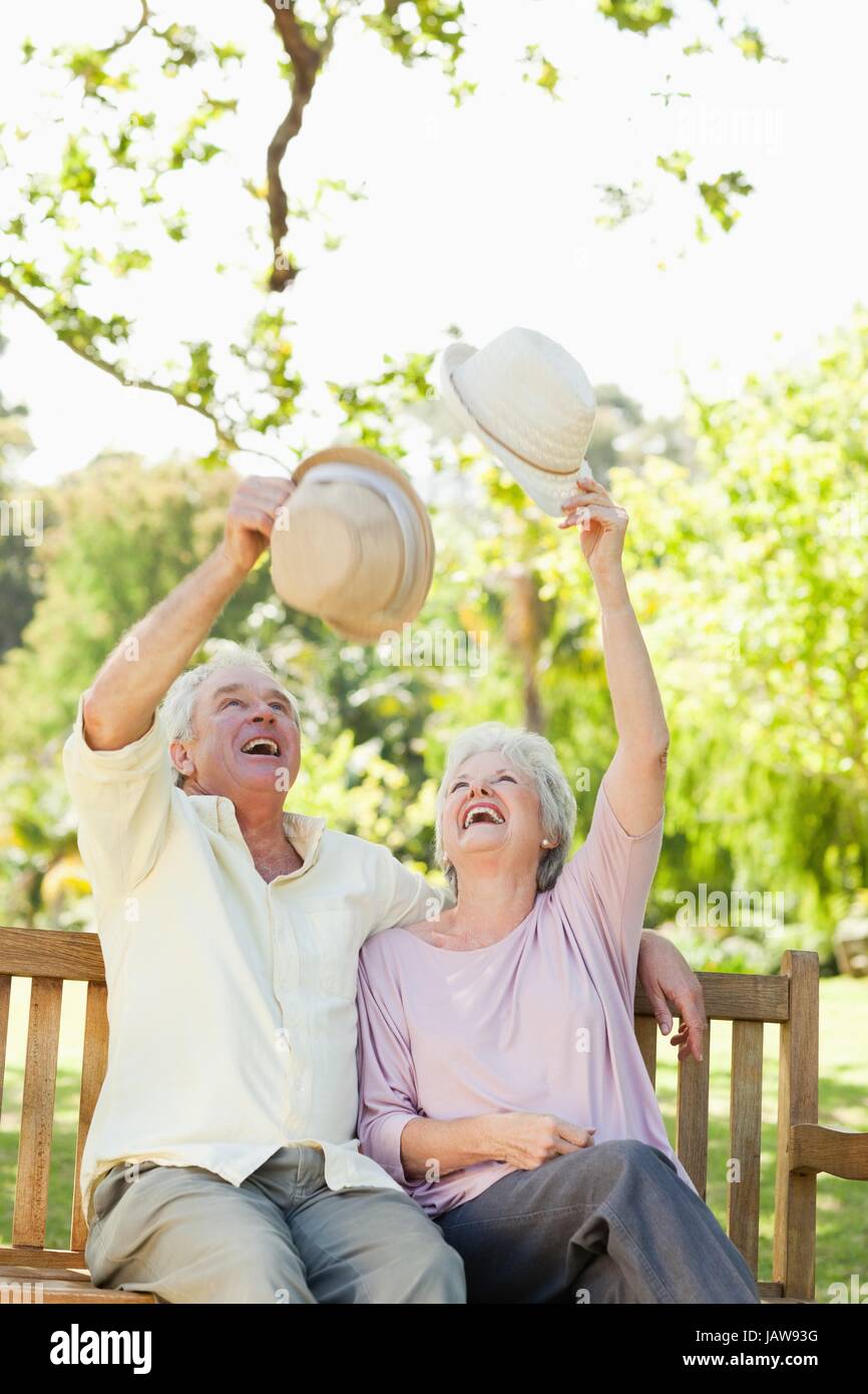 Two friends raising their hats while sitting on a bench Stock Photo - Alamy