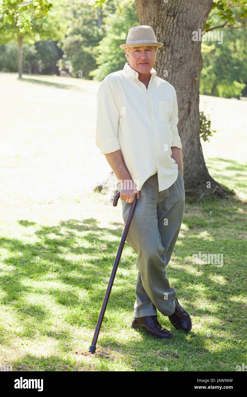 Man holding a cane while standing with his legs crossed Stock Photo - Alamy