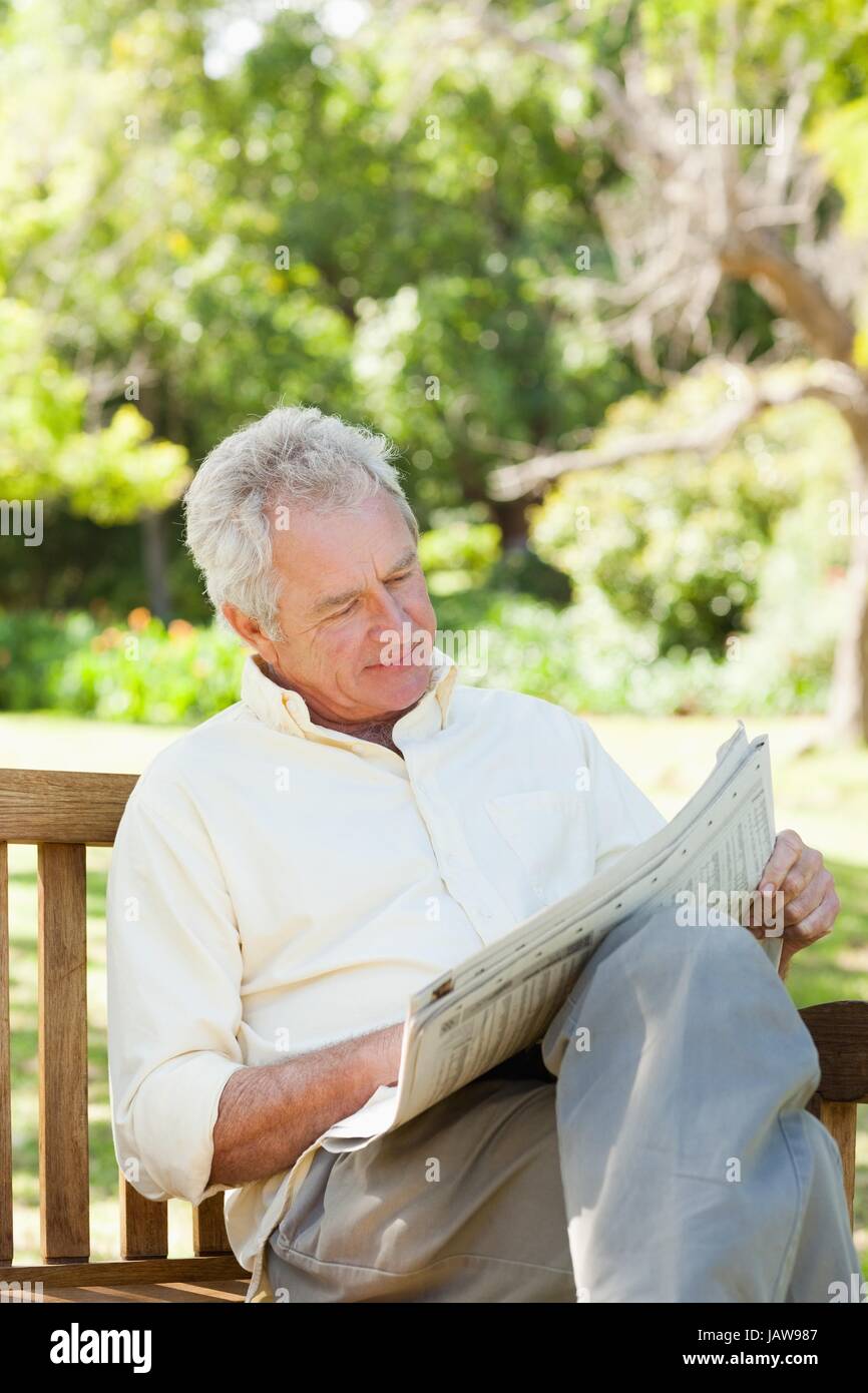 Man looking at a newspaper while sitting on a bench Stock Photo - Alamy