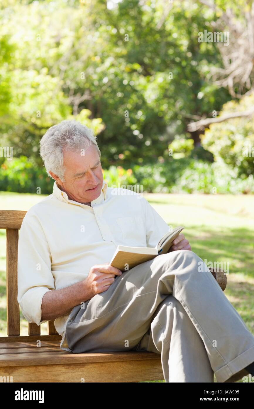 Man smiling while reading a book on a bench Stock Photo - Alamy