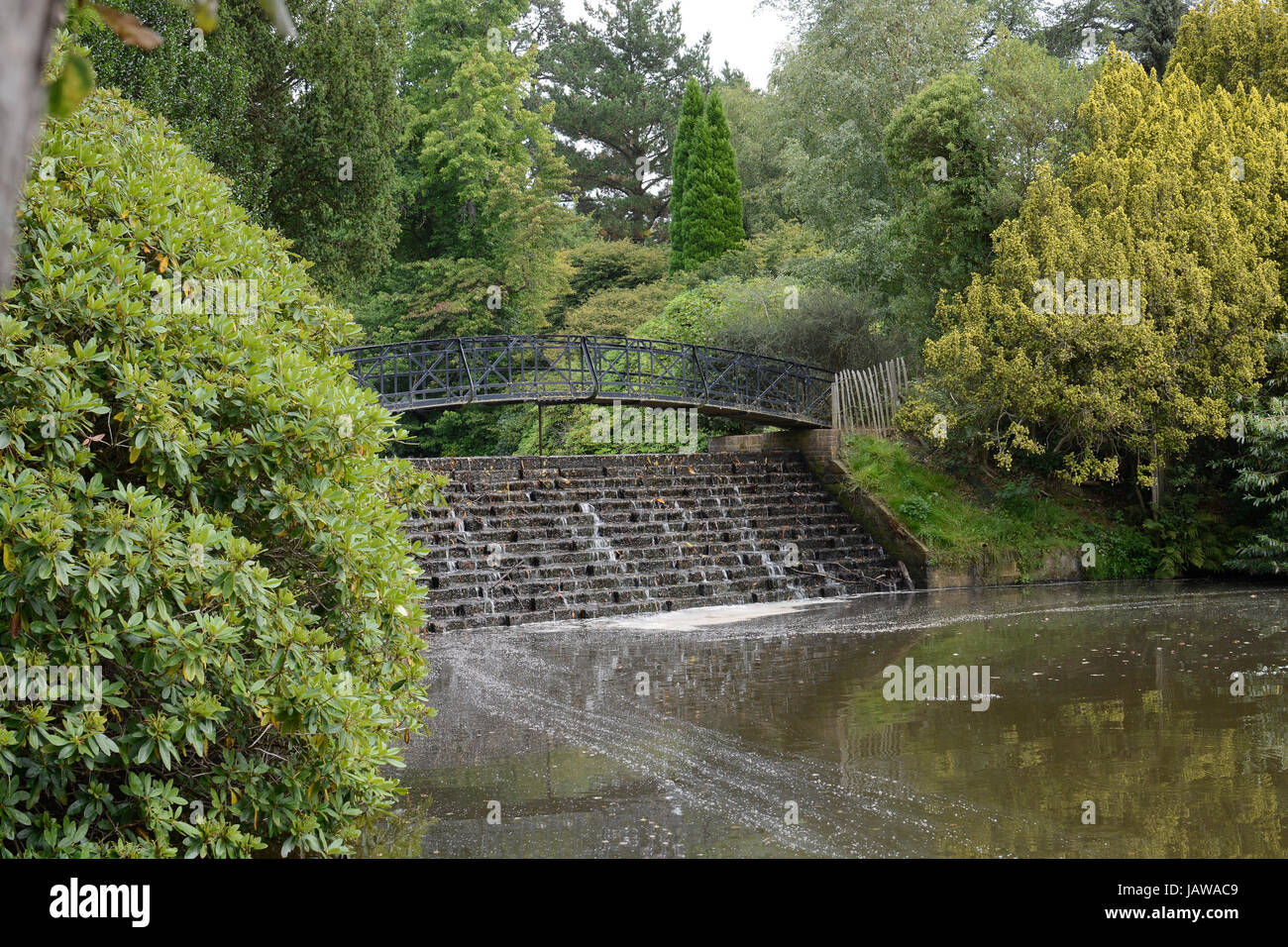 Ironwork bridge over small waterfall by lake in an English country ...