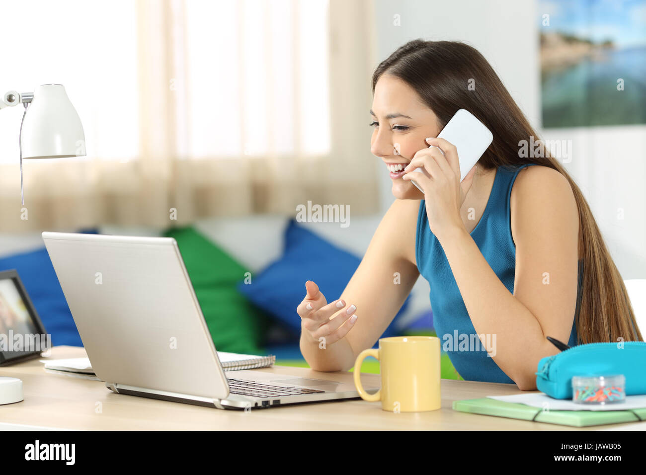 Beautiful happy student talking on mobile phone in a desk in her room ...