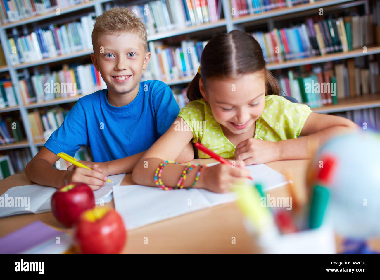 Portrait of two schoolkids sitting in library and making notes, little ...