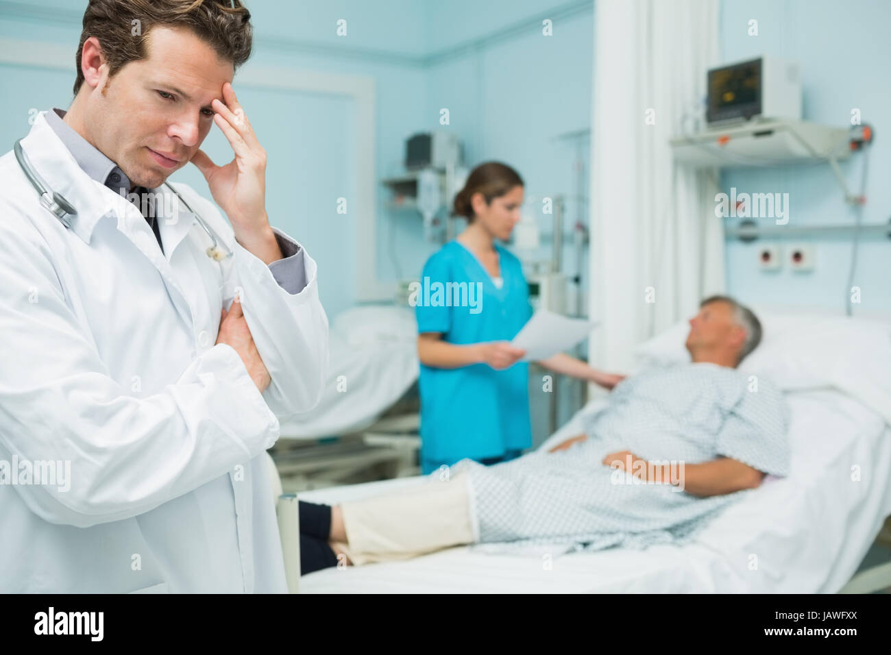 Thinking male doctor with standing in the foreground of a hospital room ...