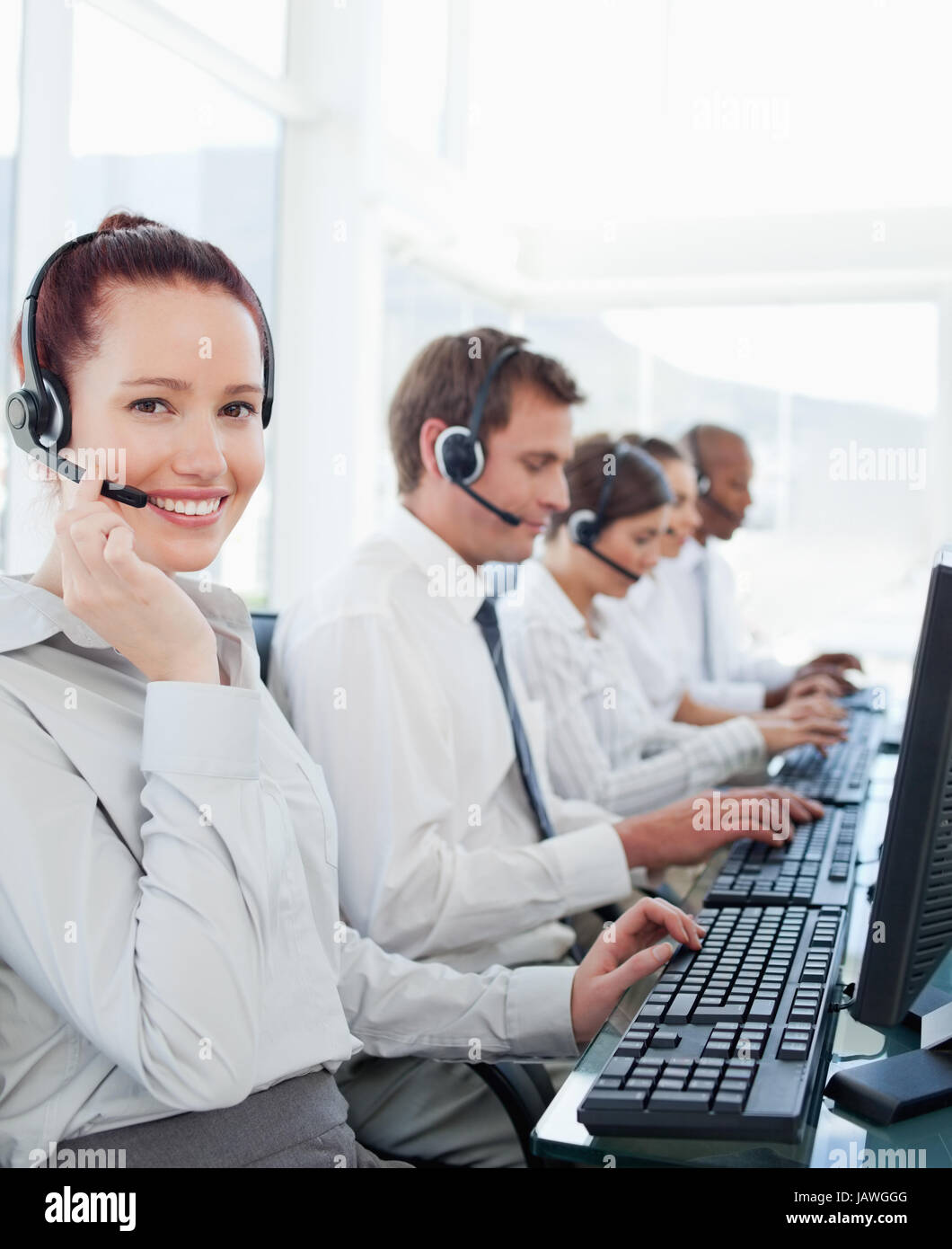 Smiling call center employee sitting with her colleagues behind her ...