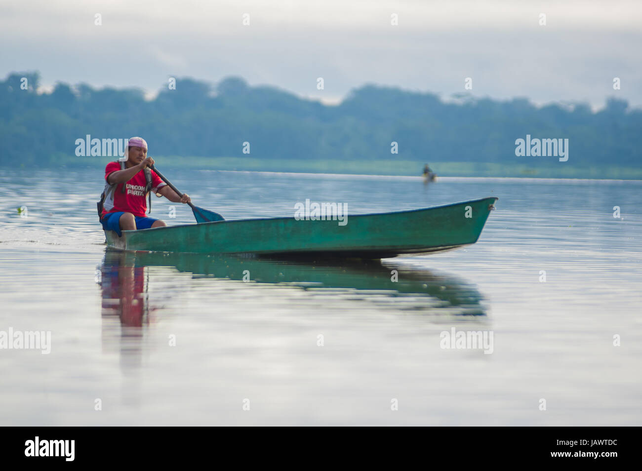 Native man paddling in his old fishing wooden boat in a calm lake water ...