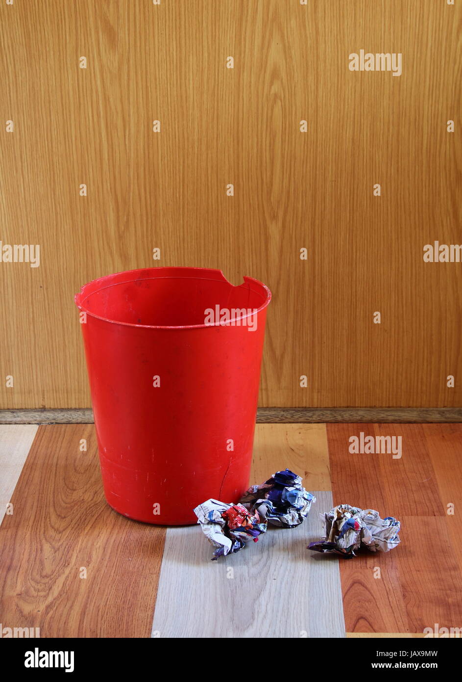 Tired looking red plastic dustbin on a wooden floor in an office with ...