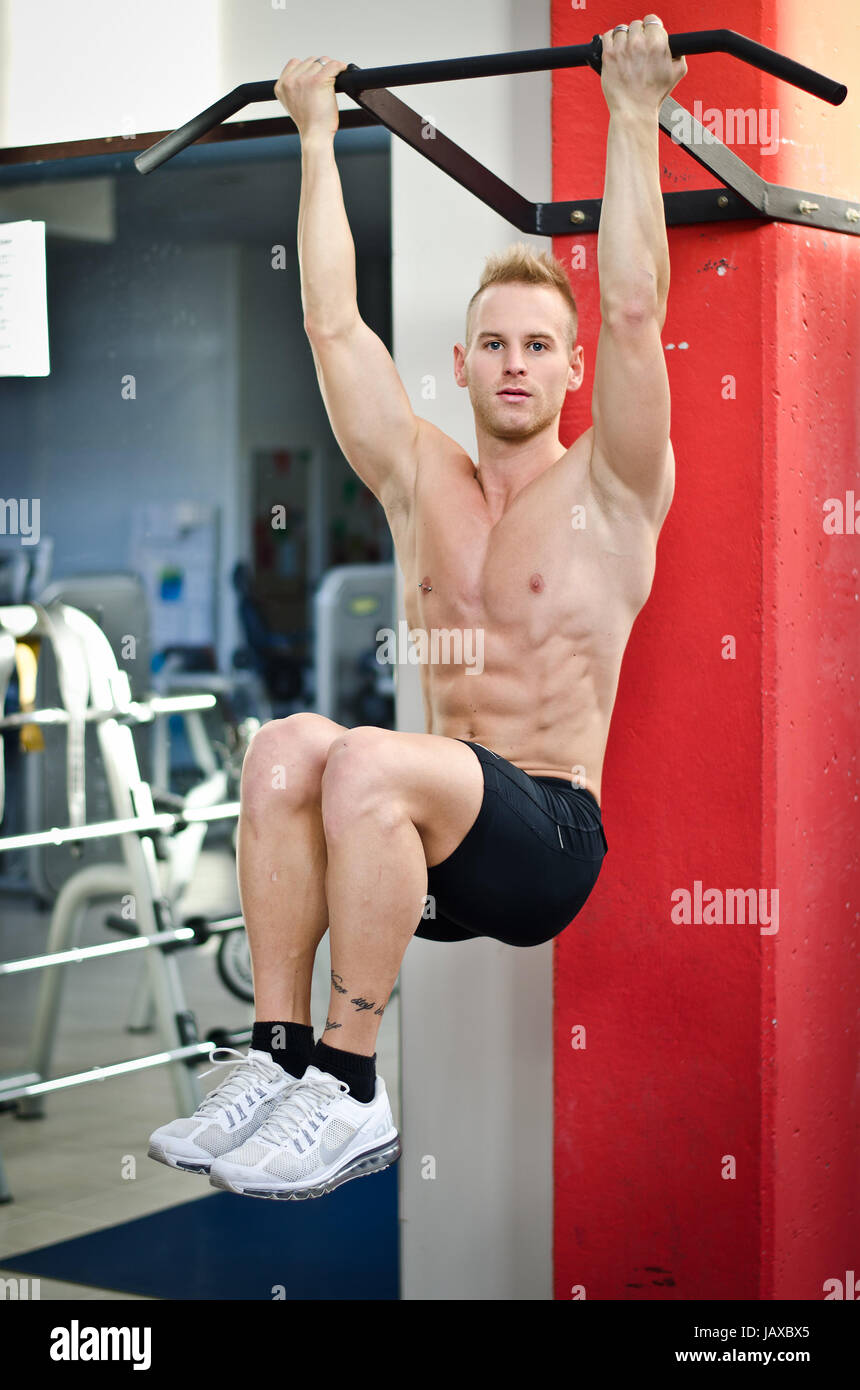 Blond, attractive young man hanging from gym equipment, looking at ...