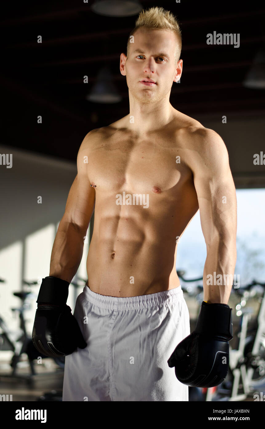 Attractive shirtless young man with boxing gloves, looking at camera ...
