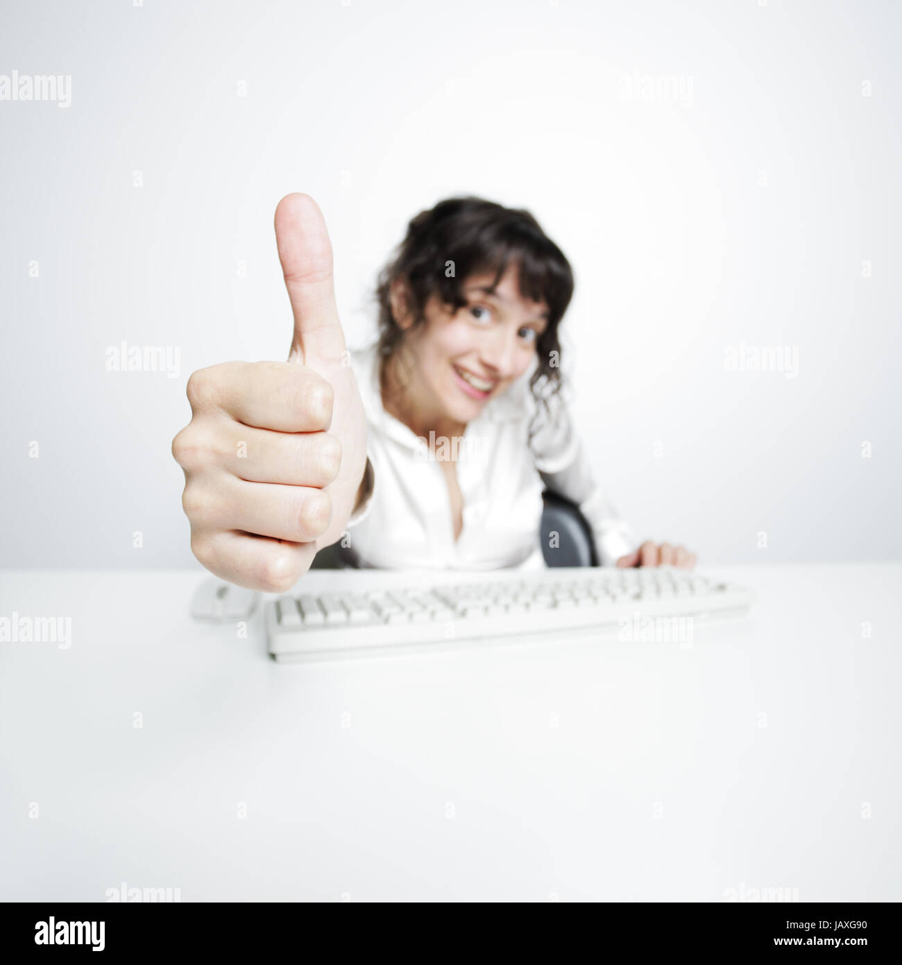 thumbs up shown by a happy, smiling young woman working at her office ...