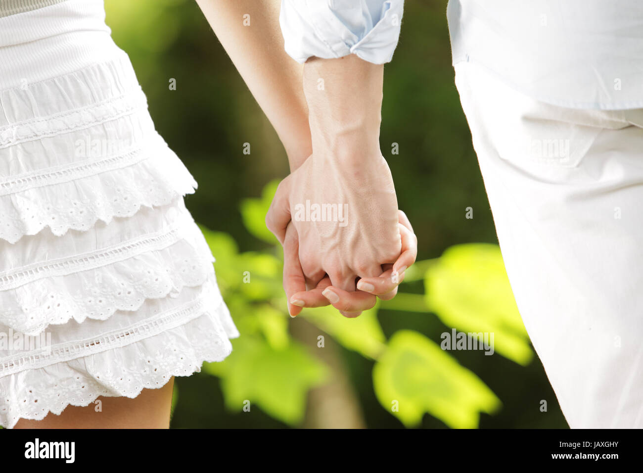 a couple of young lovers strolling holding hands in a park, close up of ...