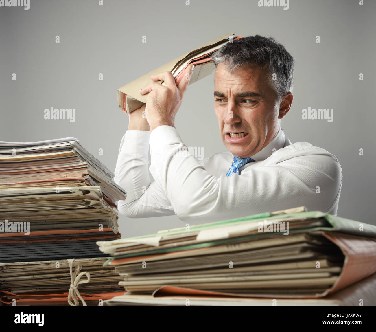 Stressed businessman, with a too much paperwork and files piled up on ...