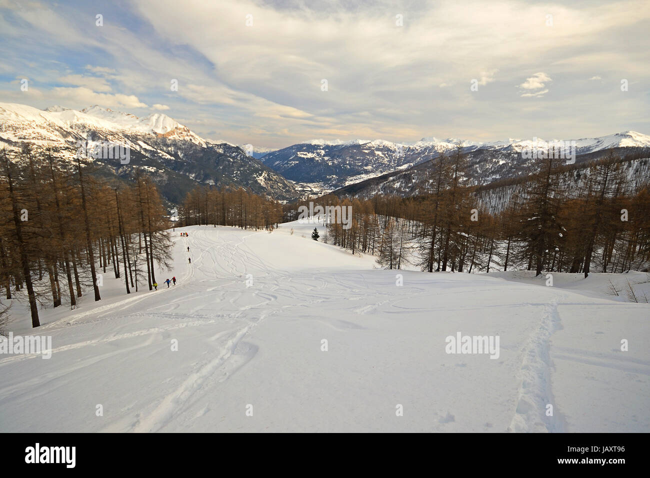 Off piste ski slope with ski tracks, some hikers and scenic valley in ...