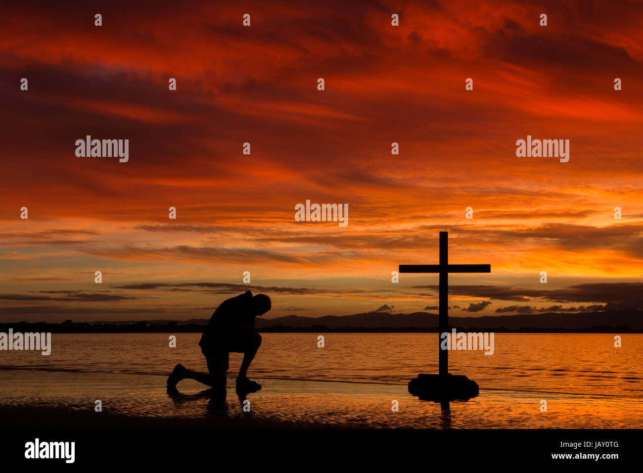 Man kneeling by a cross as the sun lights up the dawn sky Stock Photo ...