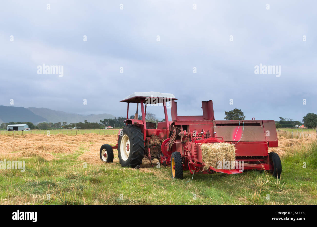 Red tractor with a red hay baler ready to bale up some dry hay Stock ...