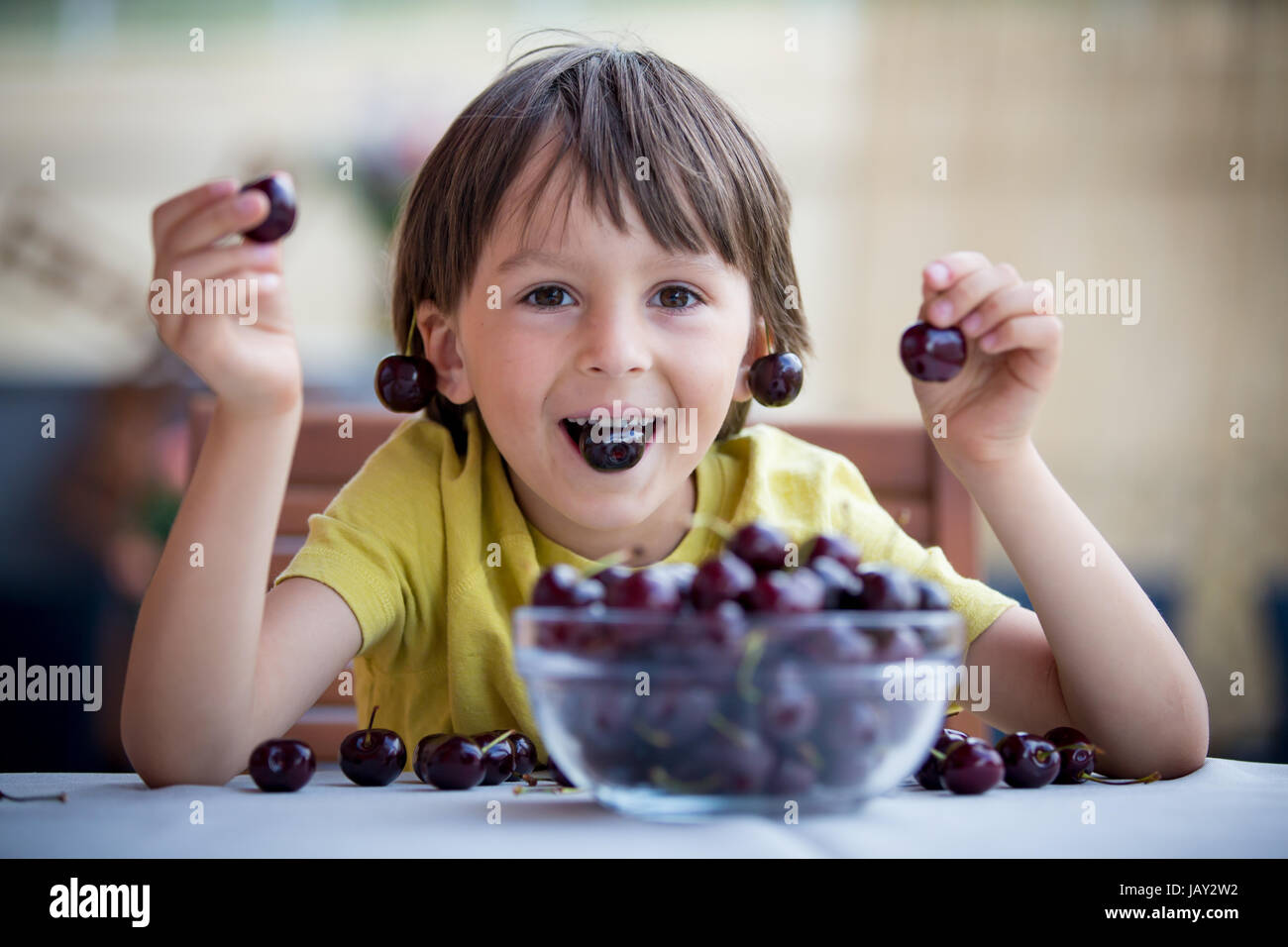 Cute little boy, eating sweet cherry outdoors, sitting on table Stock ...