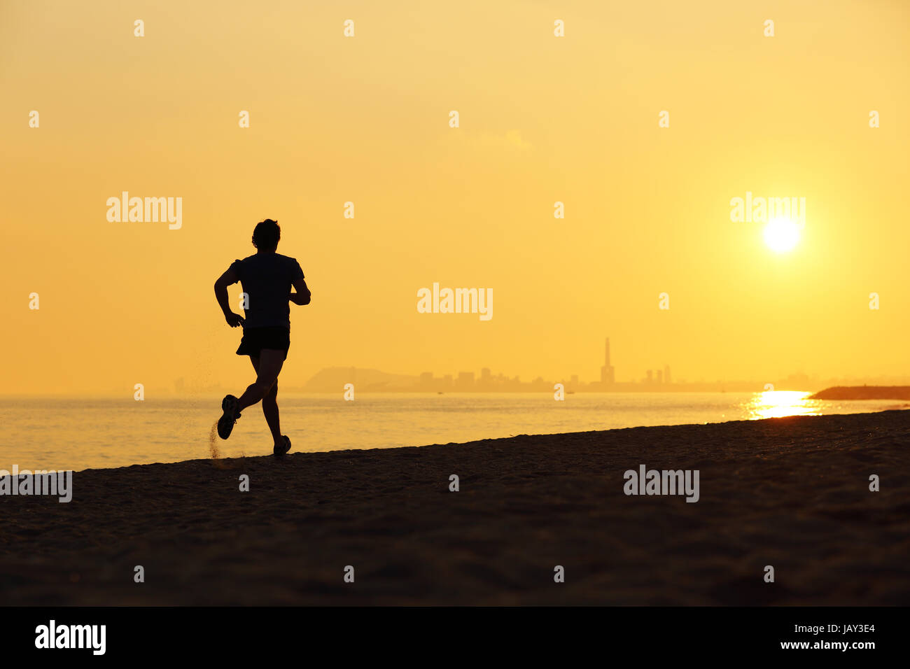 Jogger silhouette running on the beach at sunset with the horizon in ...
