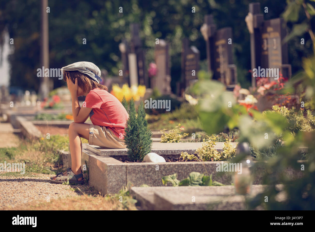 Sad little boy, sitting on a grave in a cemetery, feeling sad and ...