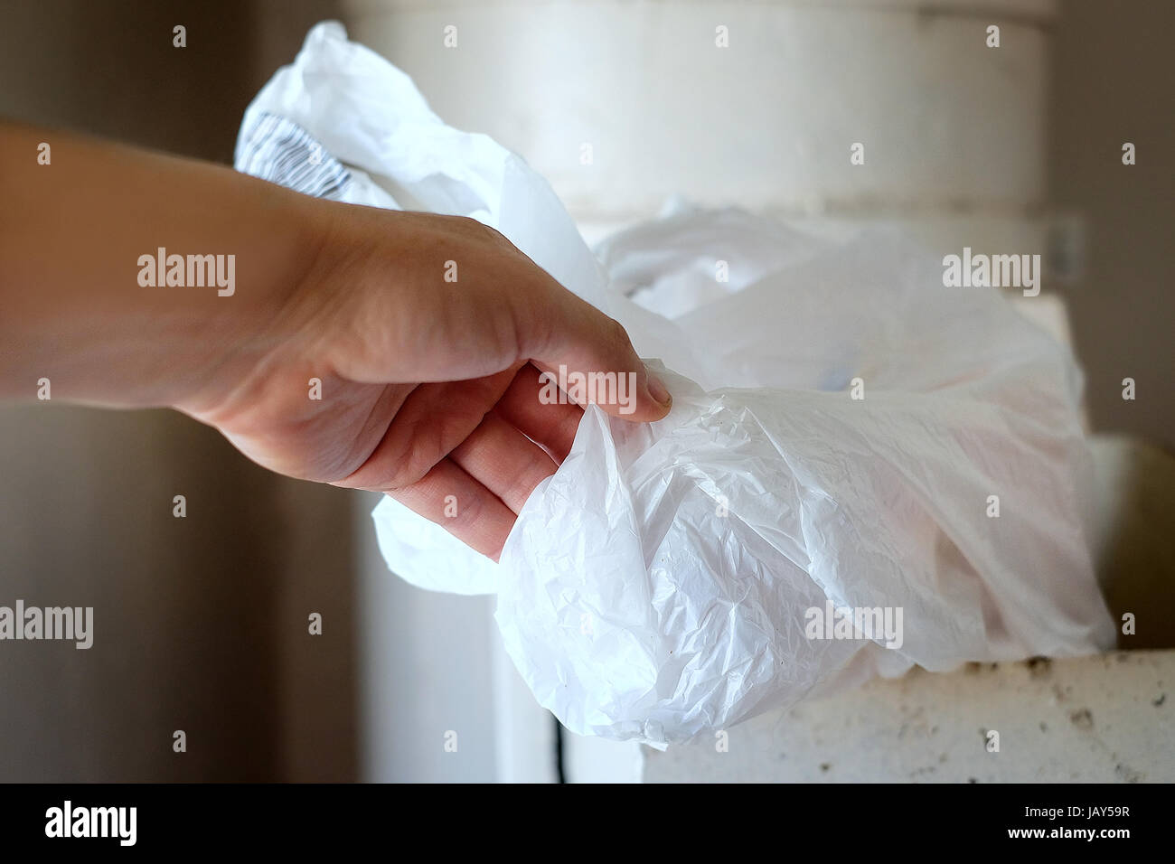 Male hand about to throw a cellophane bag into a disposal bin, closeup ...