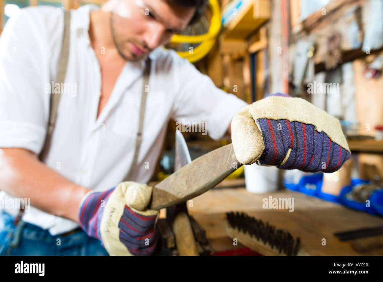 Young man in the Bavarian mountains grinds his axe and sharpening tools ...