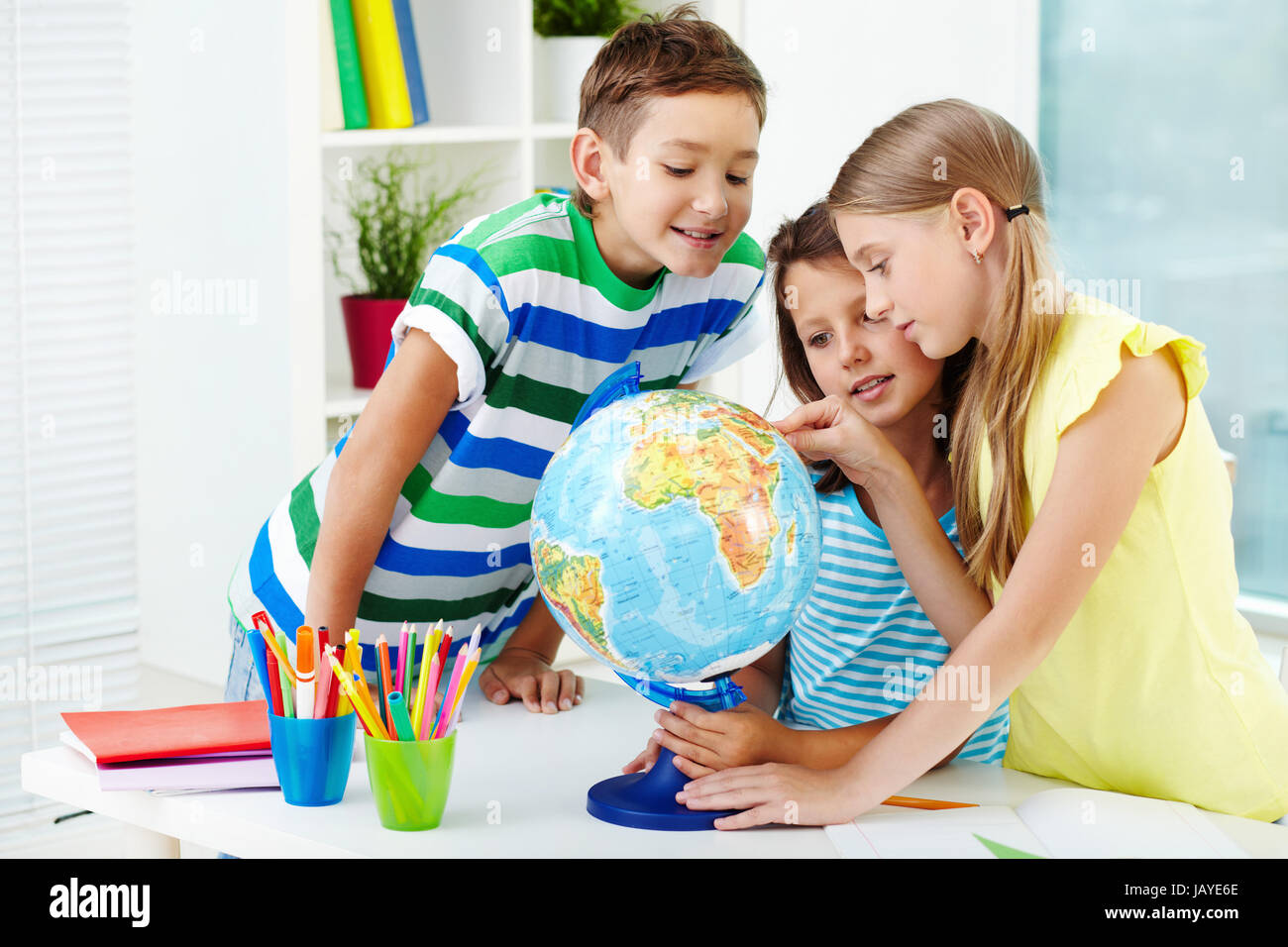 Portrait of happy classmates at workplace studying globe in classroom ...