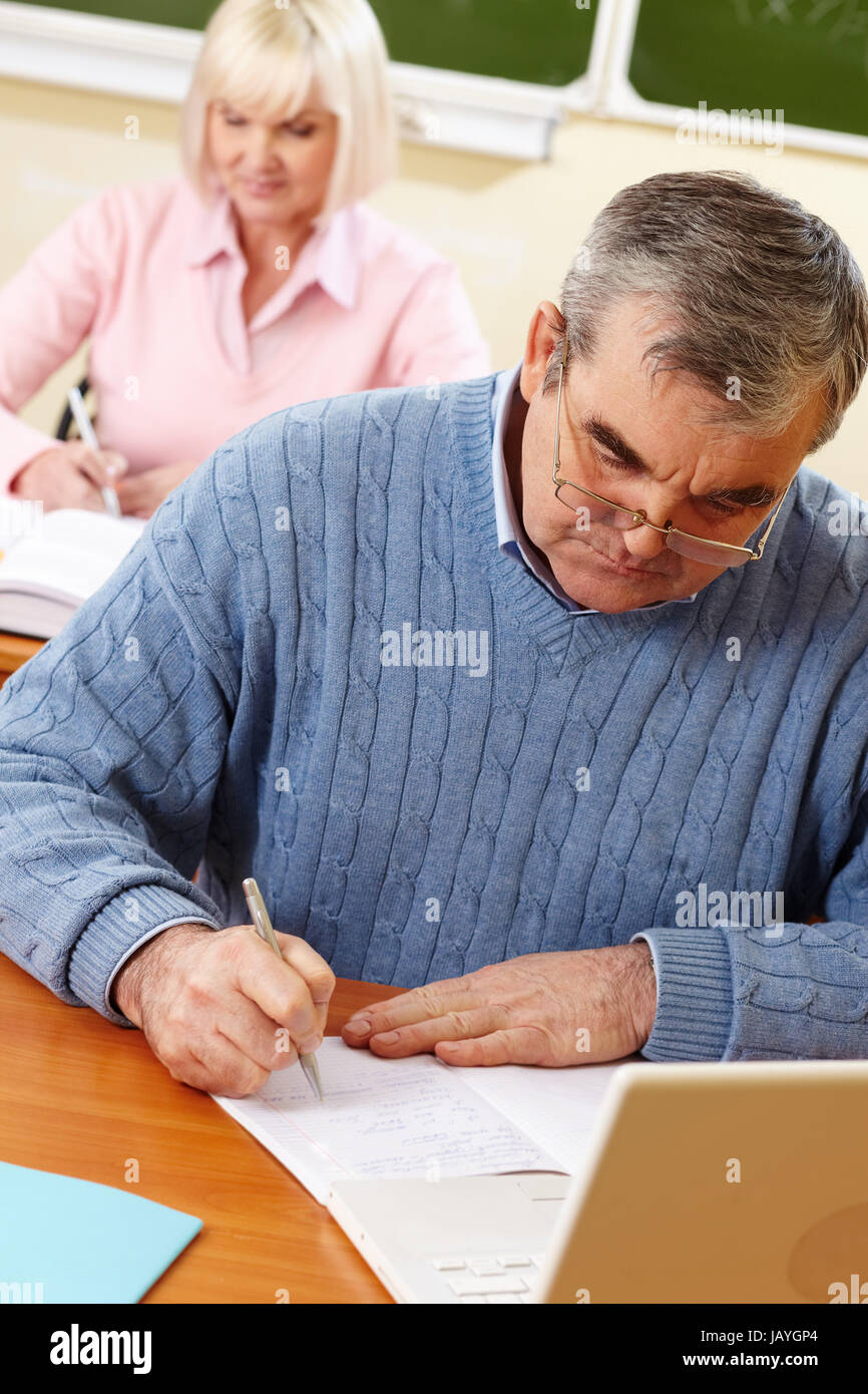 Senior man doing the task in classroom with his classmate on background ...