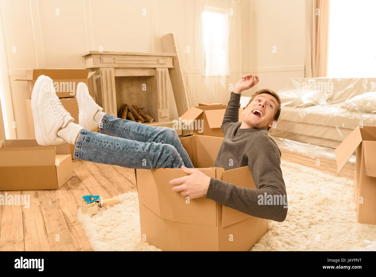 side view of cheerful man sitting in cardboard box at new home Stock ...