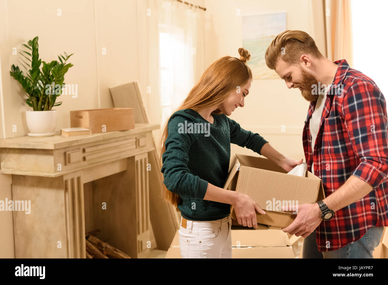 side view of young smiling couple looking into cardboard box at new ...