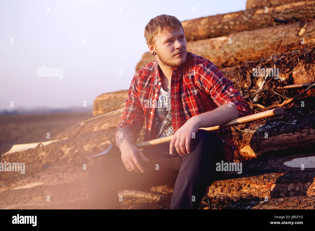 Sad young bearded lumberjack man carrying an axe on arms and looking at ...