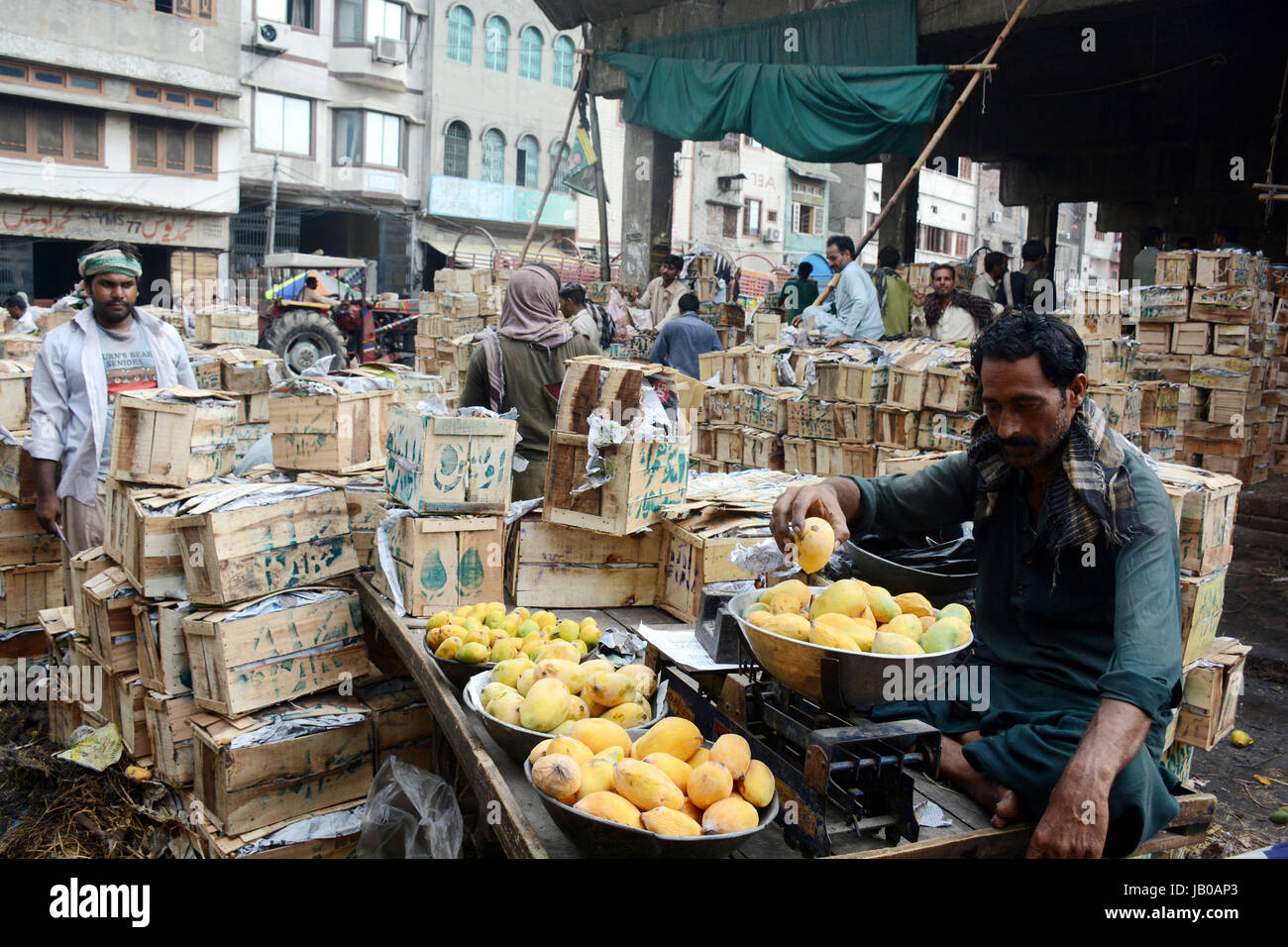 Lahore. 8th June, 2017. A vendor weighs mango at a fruit market in ...