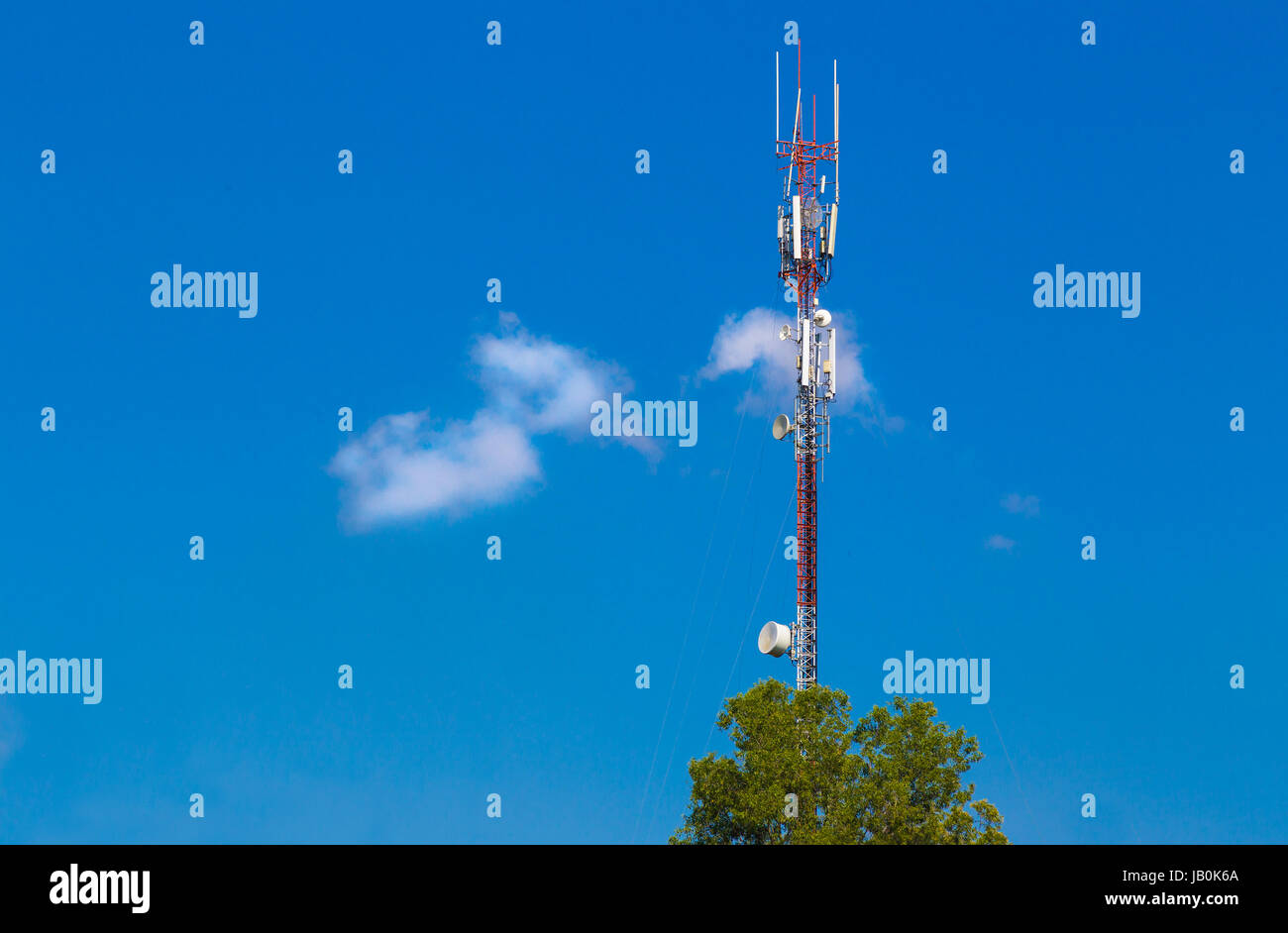 skinny tall telecommunication tower against deep blue sky and white fluffy clouds with ...