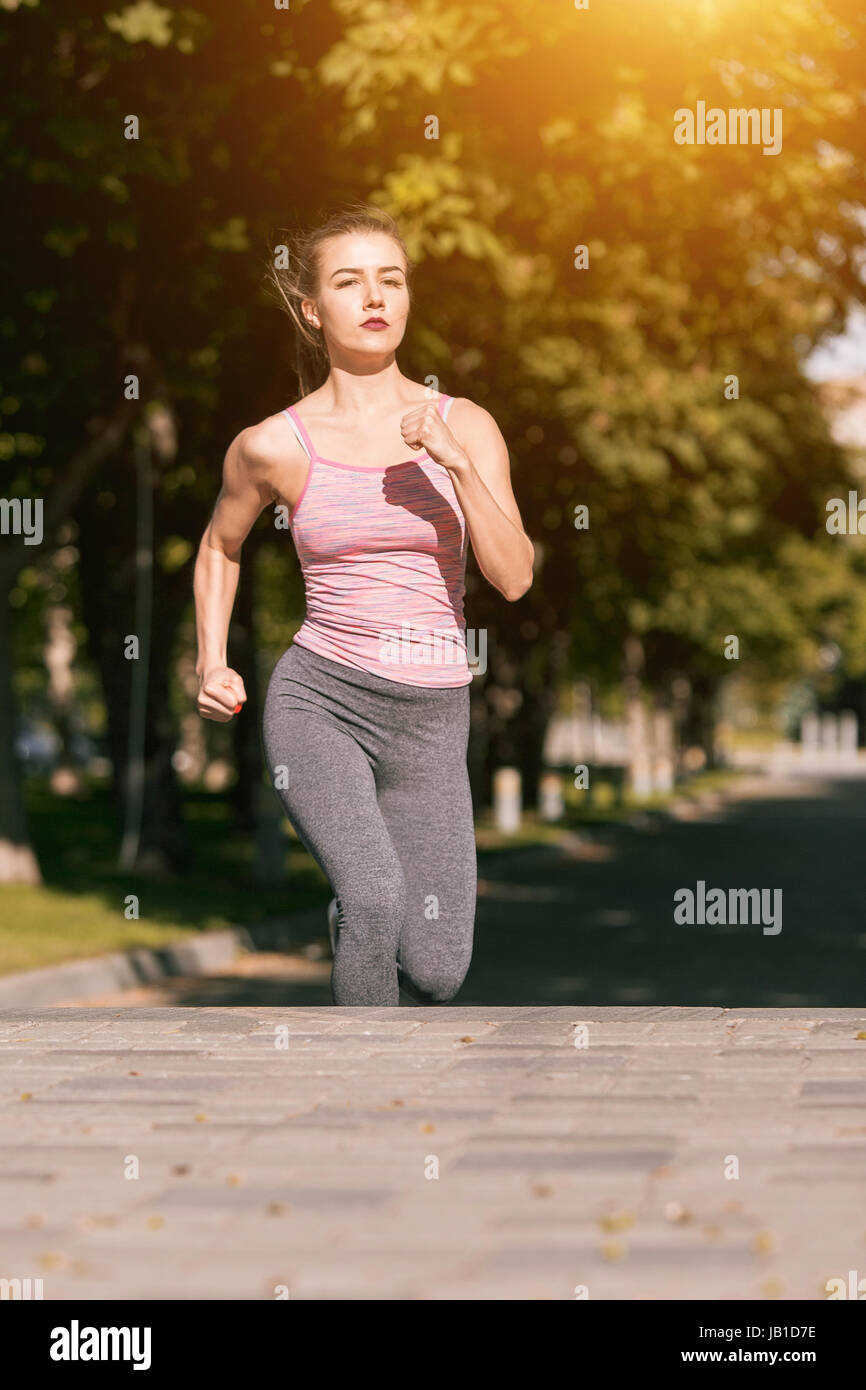 Pretty sporty woman jogging at park in sunrise light Stock Photo - Alamy